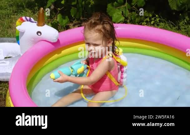A child in the pool in the yard shoots water from a water pistol. A toy ...