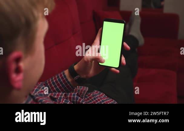 Back view close up man hands holding chromakey green screen smartphone watching content, play ...
