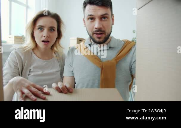 Portrait of surprised young couple opening box looking inside with ...
