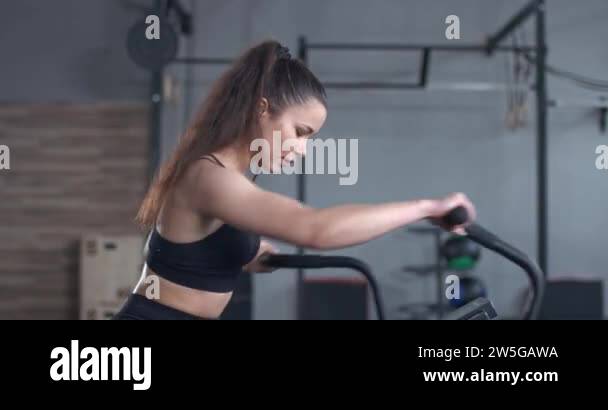 Female in the gym, young woman trains on a elliptical bike simulator ...