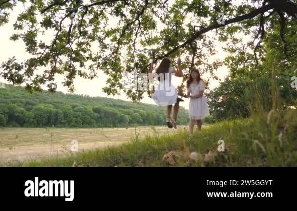 Happy young mother shakes a teenage girl on a swing. Mom and daughter ...