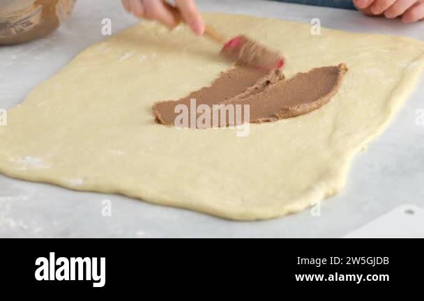 Beautiful female hands smear the dough with cinnamon butter for making ...