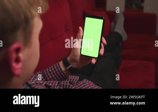 Back view close up man hands holding chromakey green screen smartphone watching content, play ...