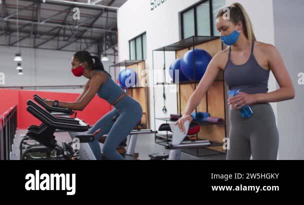 Caucasian woman disinfecting exercise bike saddle at gym. spraying with ...