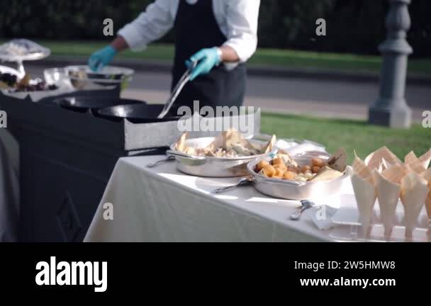 Waiter in uniform and gloves cooking outdoors during catering service ...