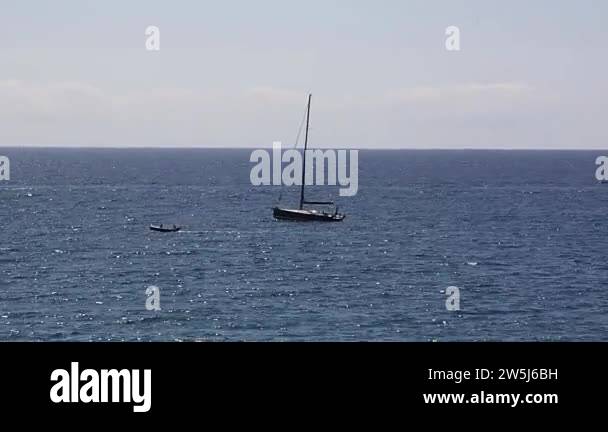 sailboat lulled by the waves with dinghy moving away on the horizon ...