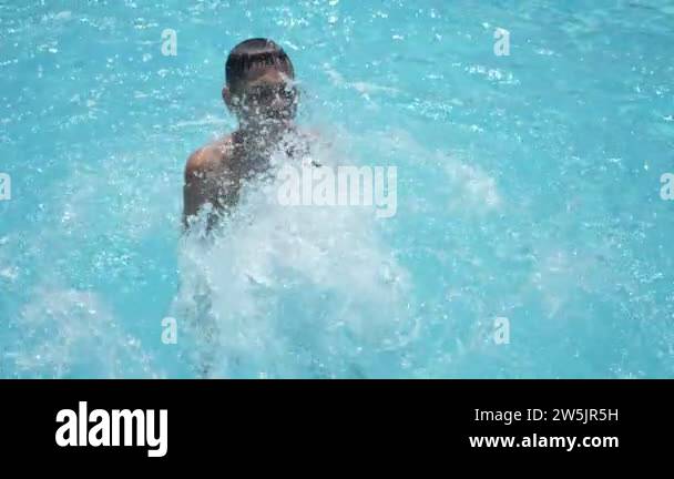 Happy guy smiling and jumping in a swimming pool with splashing in slow ...
