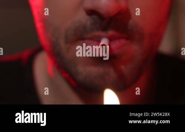 Man lighting a cigarette and smoking at a table in bar with red light ...