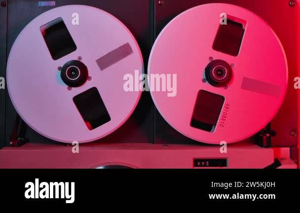 Old coil tape recorder with magnetic tape on reels illuminated by red ...