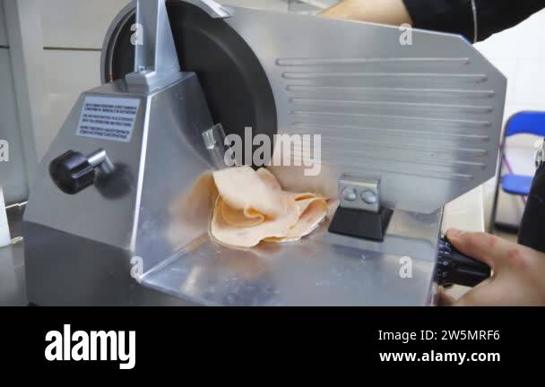 Close up arm of cook chopping sausage on electric food slicer at ...