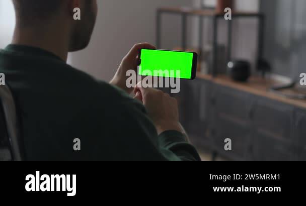 male user is swiping and tapping on touch screen of modern smartphone, holding gadget ...