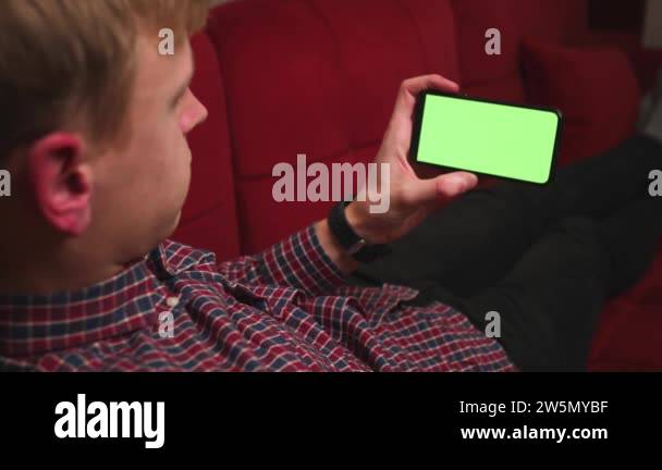 Back view close up man hands holding chromakey green screen smartphone watching content, play ...