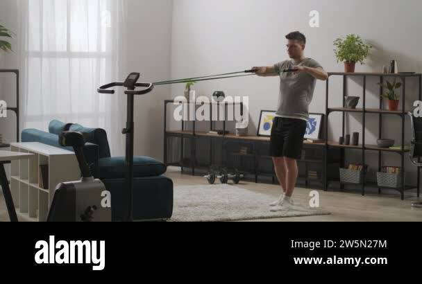 bodybuilder is training with rubber tapes in apartment, strength workout for sportsmen, home ...
