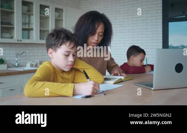 Adorable mixed race school boy writing a dictation dictated by his loving mom. Single mother ...