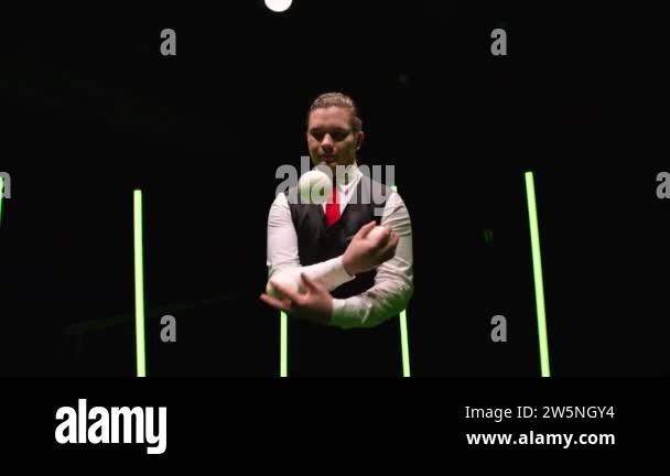 Circle movement camera around professional circus performer juggling white balls against a black ...