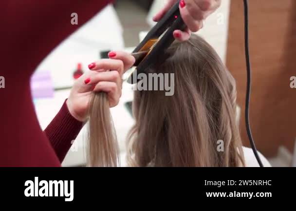 the barber's hands pinch a strand of hair with a straightener, stretch ...