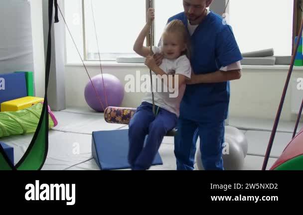 Child girl with physiotherapist swinging on swing during sensory ...
