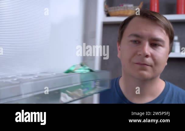 Hungry single man opens door of empty, littered refrigerator and tries ...