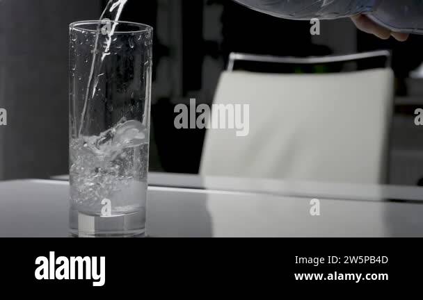 Mineral water flow into a glass glass, natural water is poured into a glass from a plastic ...