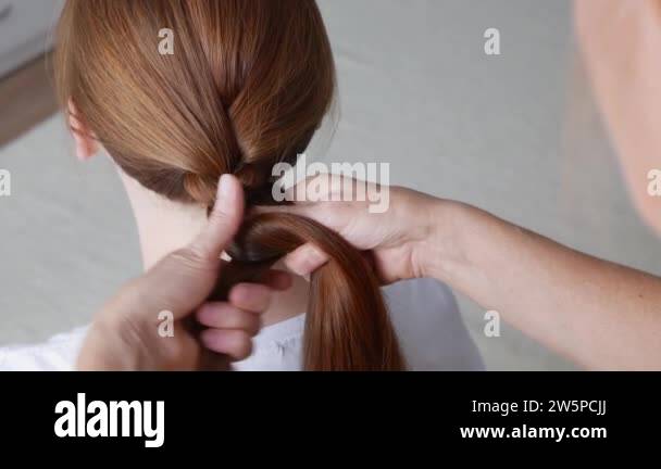 Close up view of making braid on red hair girl. Mother braids for her ...