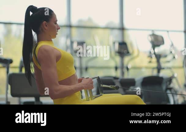 Hispanic Woman Does Exercises On The Rowing Machine A Girl Sits Behind