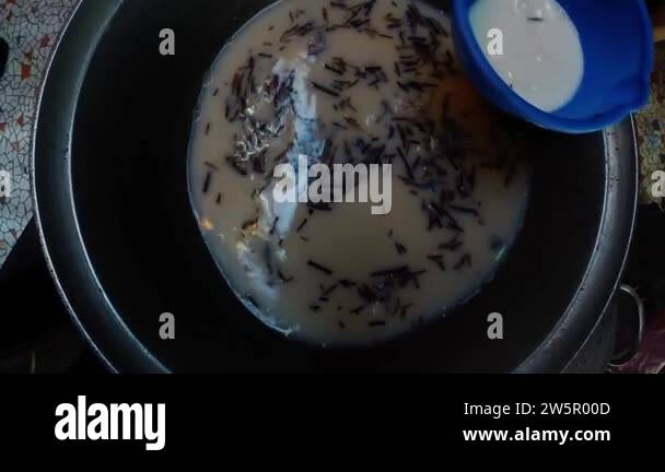 mixing pouring milk in a boiling tea in metal pan top view close-up ...