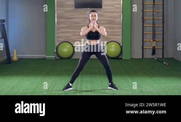 Young female performs a warm-up in the gym, a fitness coach shows and ...