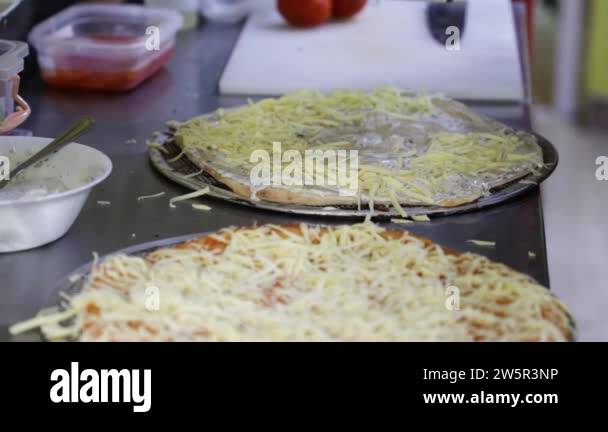 Grating cheese with a metal grater and pouring it over pizza crusts ...