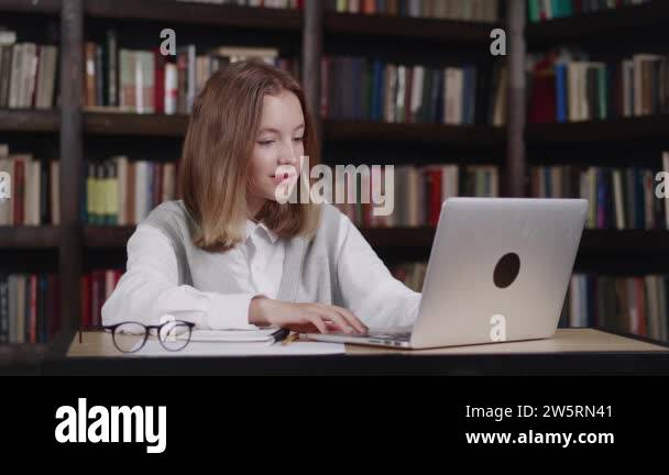 teen girl sitting in library answering teacher while having online ...