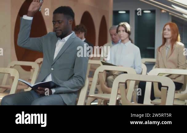 Medium shot of young African male reporter raising hand and asking ...