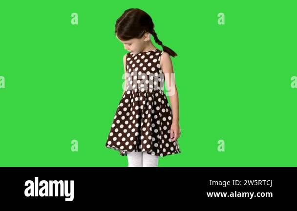 Little girl in polka dot dress looking around and down at her feet on a ...