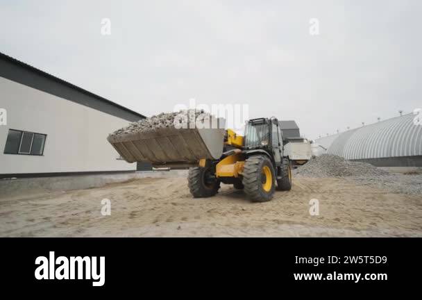 Tractor moves rubble to truck. Excavator-loader rakes rubble from pile ...