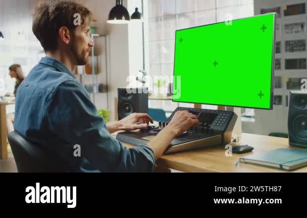 Young Professional Creative Employee Works on His Personal Computer with Big Green Screen Mock ...