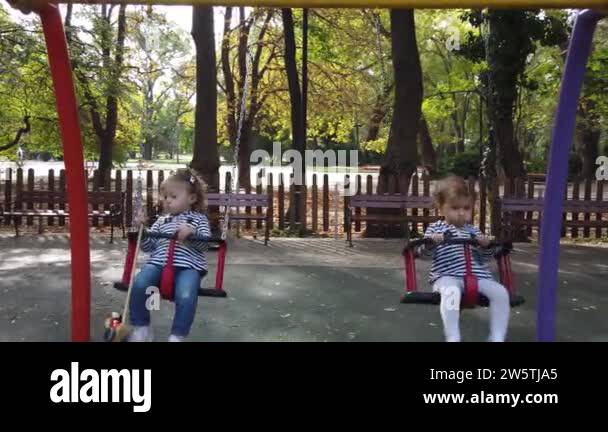 Two little girls, playing at the playground. Fraternal twins sisters, swinging on a swing Stock ...