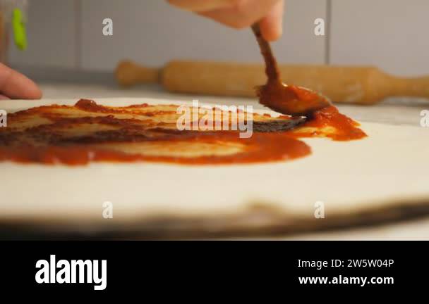 Male arm of cook applying ketchup on pizza dough using a spoon at ...