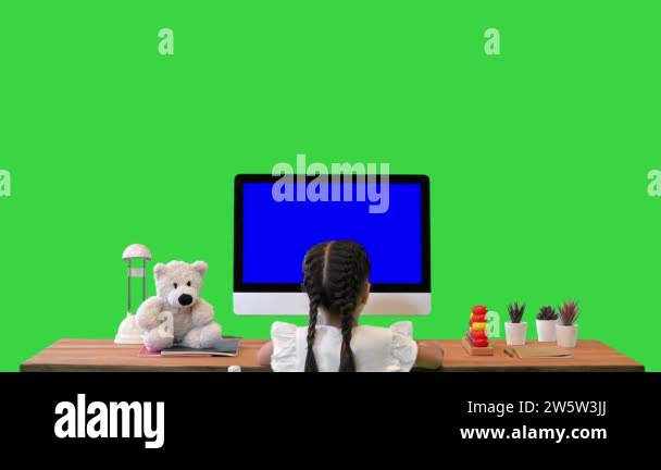 Little girl sitting at the desk and watching something on a monitor ...