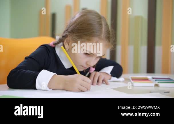 Portrait of unhappy girl drawing at desk and throwing pencil away. Cute ...