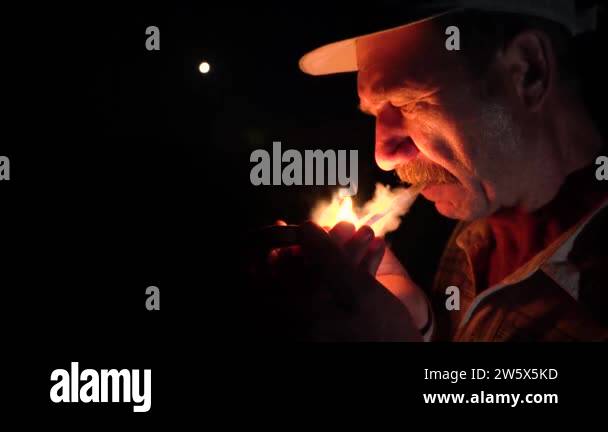 A man lights a cigarette at night on the street in the dark.Night ...