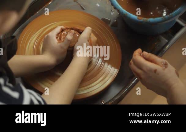 A potter shows a young student how to properly hold a piece of clay on ...