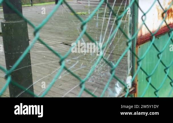 Broken window glass with shards and cracks close up behind a chain link ...