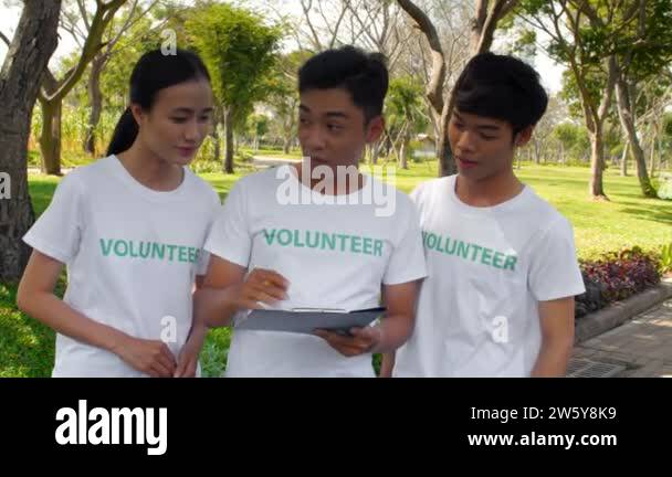 Medium shot of three Asian volunteers standing together in park and ...