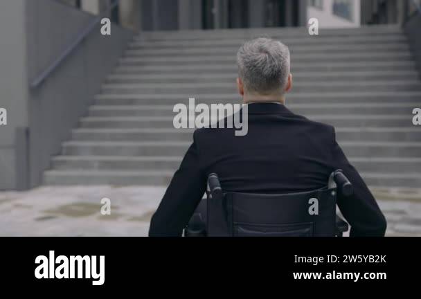 Backside view of male person in suit pushing himself on wheel chair at ...