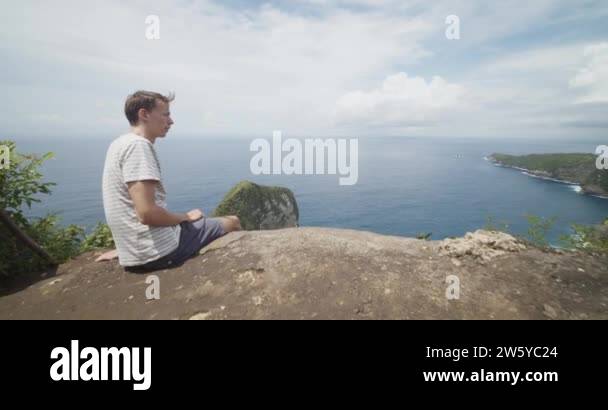 Low dolly shot of a male tourist sitting above the T-Rex Bay peninsula ...