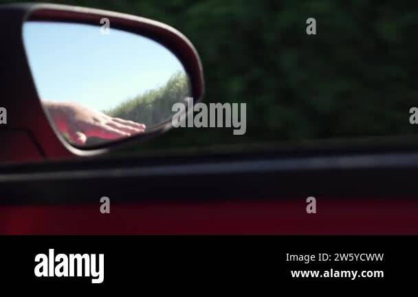 Reflection on car side mirror of mans hand floating in the wind as she ...