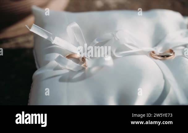 Two golden wedding rings on small white lace pillow tied with ribbons ...