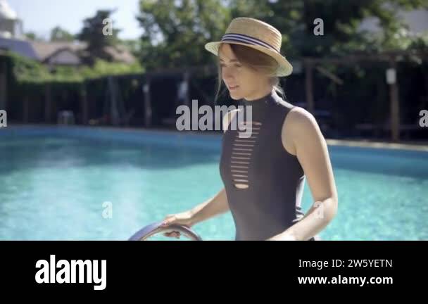 Beautiful young woman enters the pool, holding the pool ladder ...