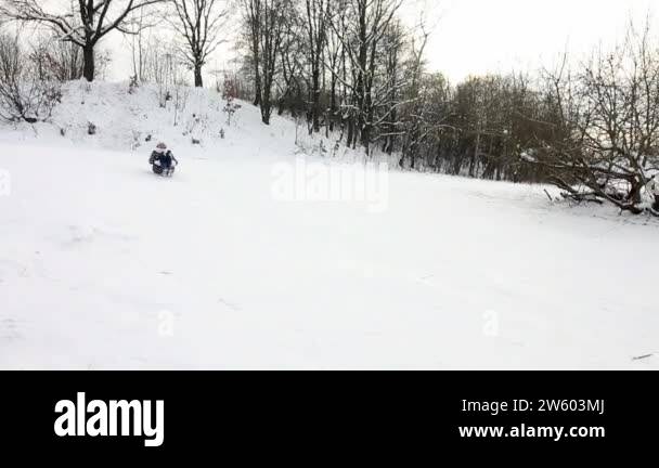 The girl climbs a snow-covered hill, sits on a sled and slides down to ...