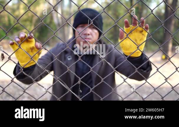 footage of a man standing by the mesh fence and his hands holding on to ...