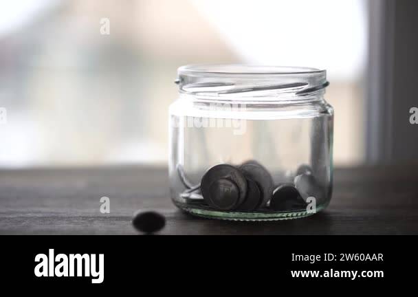 Ukrainian coins falling into the glass jar on wooden table near window ...