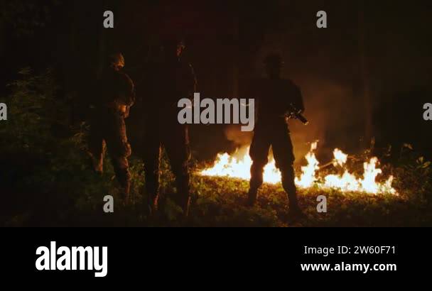 Backlit silhouette of special forces marine operators in forest on fire ...